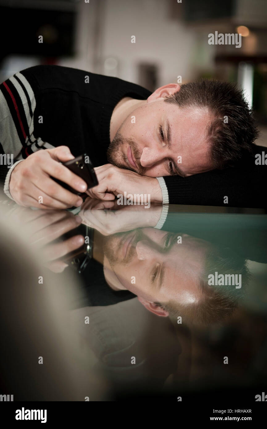 Model released, Frustrierter, junger Mann sitzt mit Handy am Tisch ...