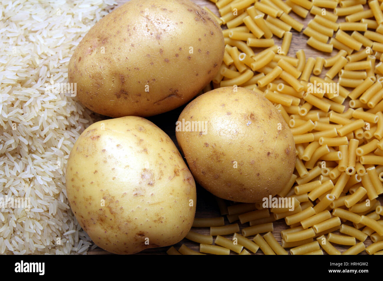 Rice, potatoes and macaroni pasta on a wooden table.Three common ...