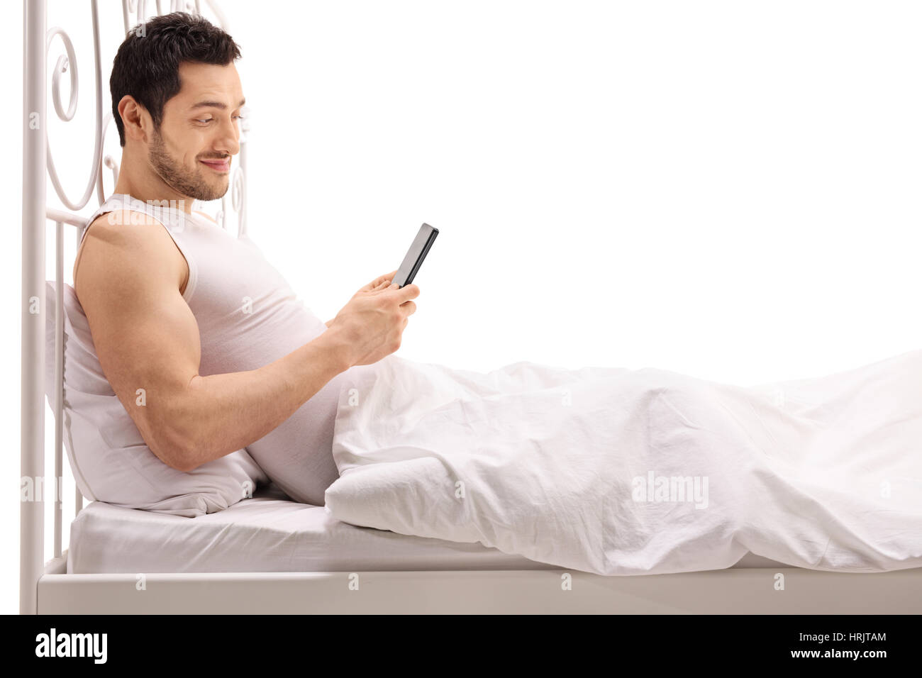 Young man using a phone while lying in bed isolated on white background ...