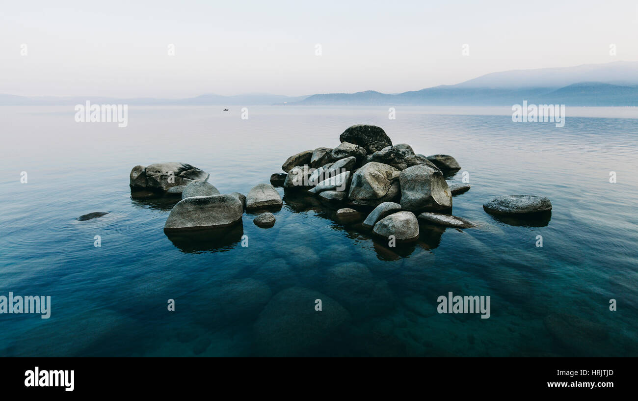 A pile of stones rising above the water level in a lake in a misty ...