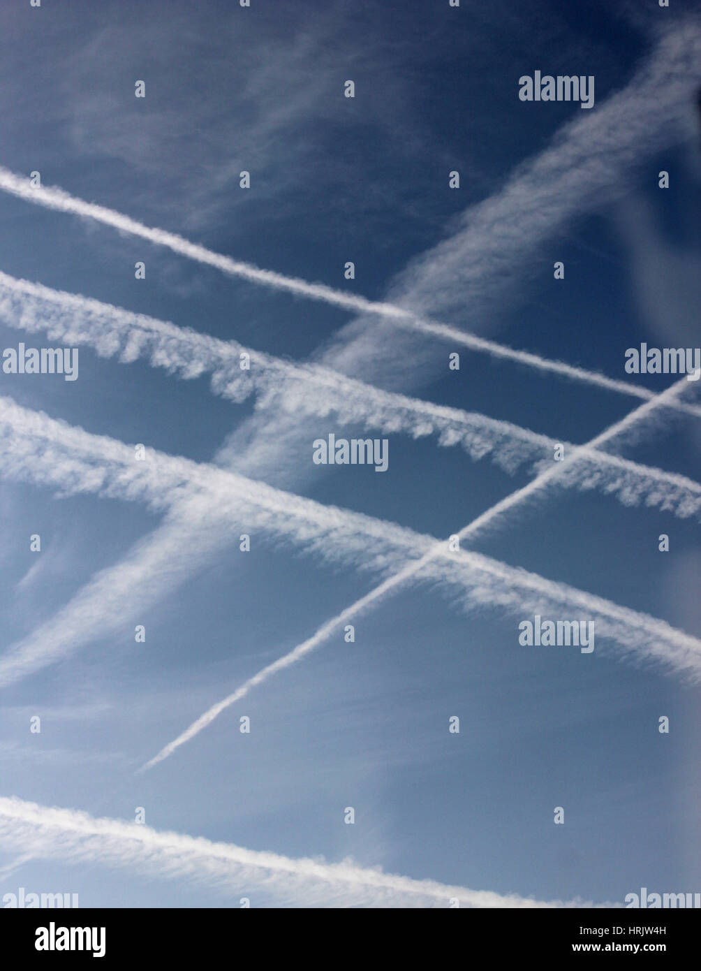 Multiple contrails crossing against blue sky and cirrus cloud and ...