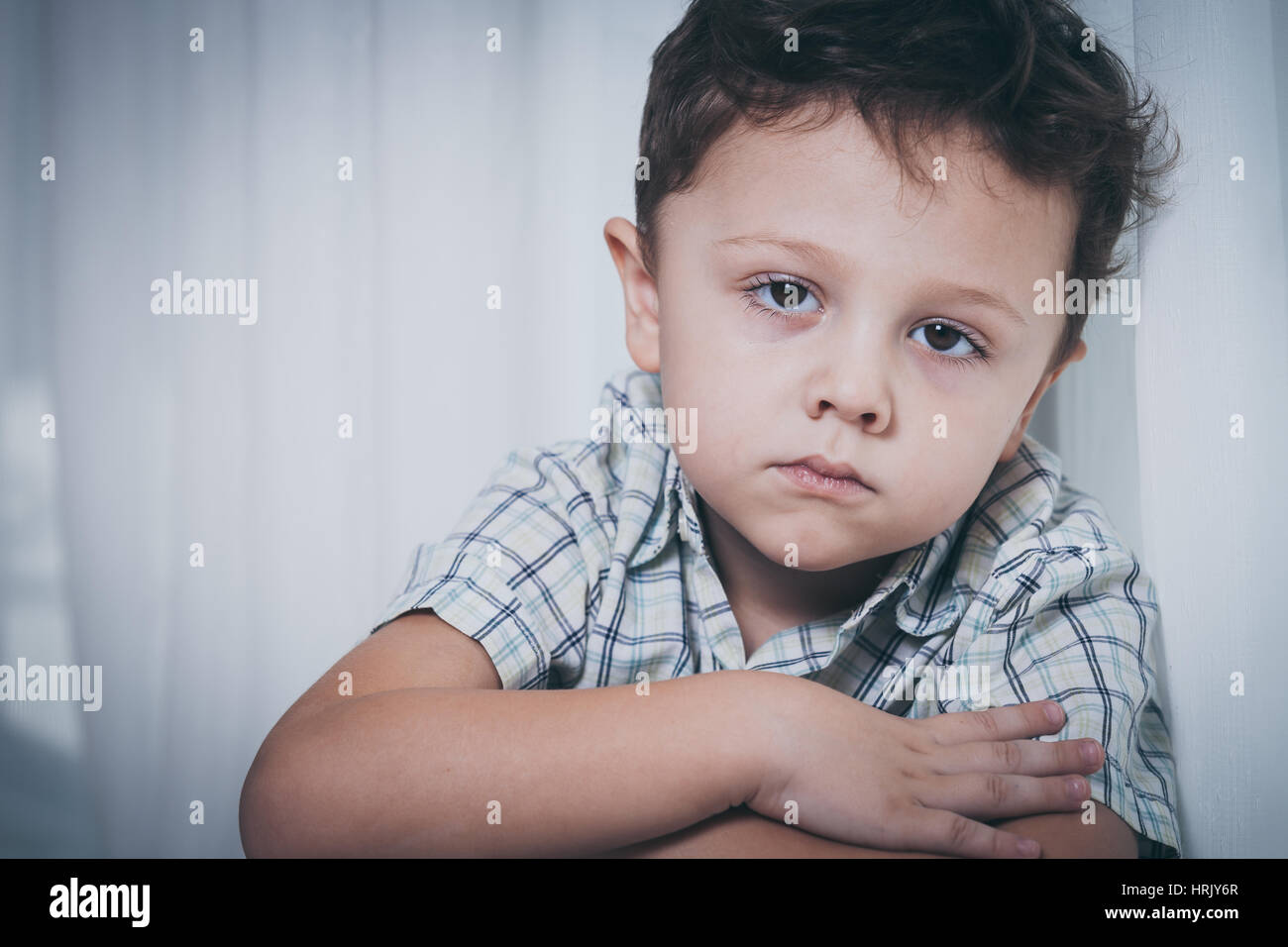 Portrait of sad little boy sitting near the window at home at the day ...