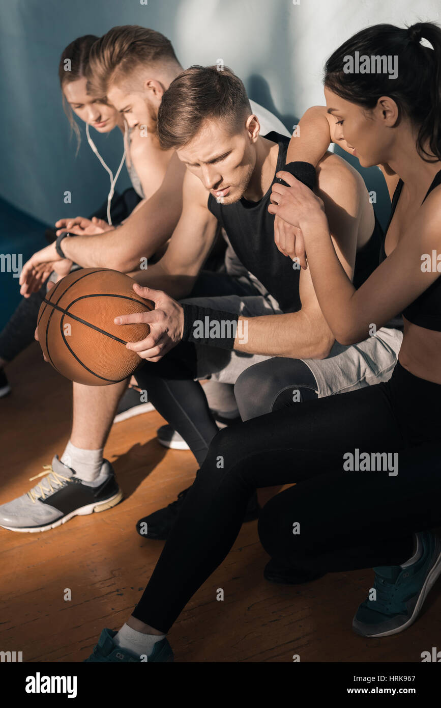 side view of sporty men and women sitting on bench in gym Stock Photo ...