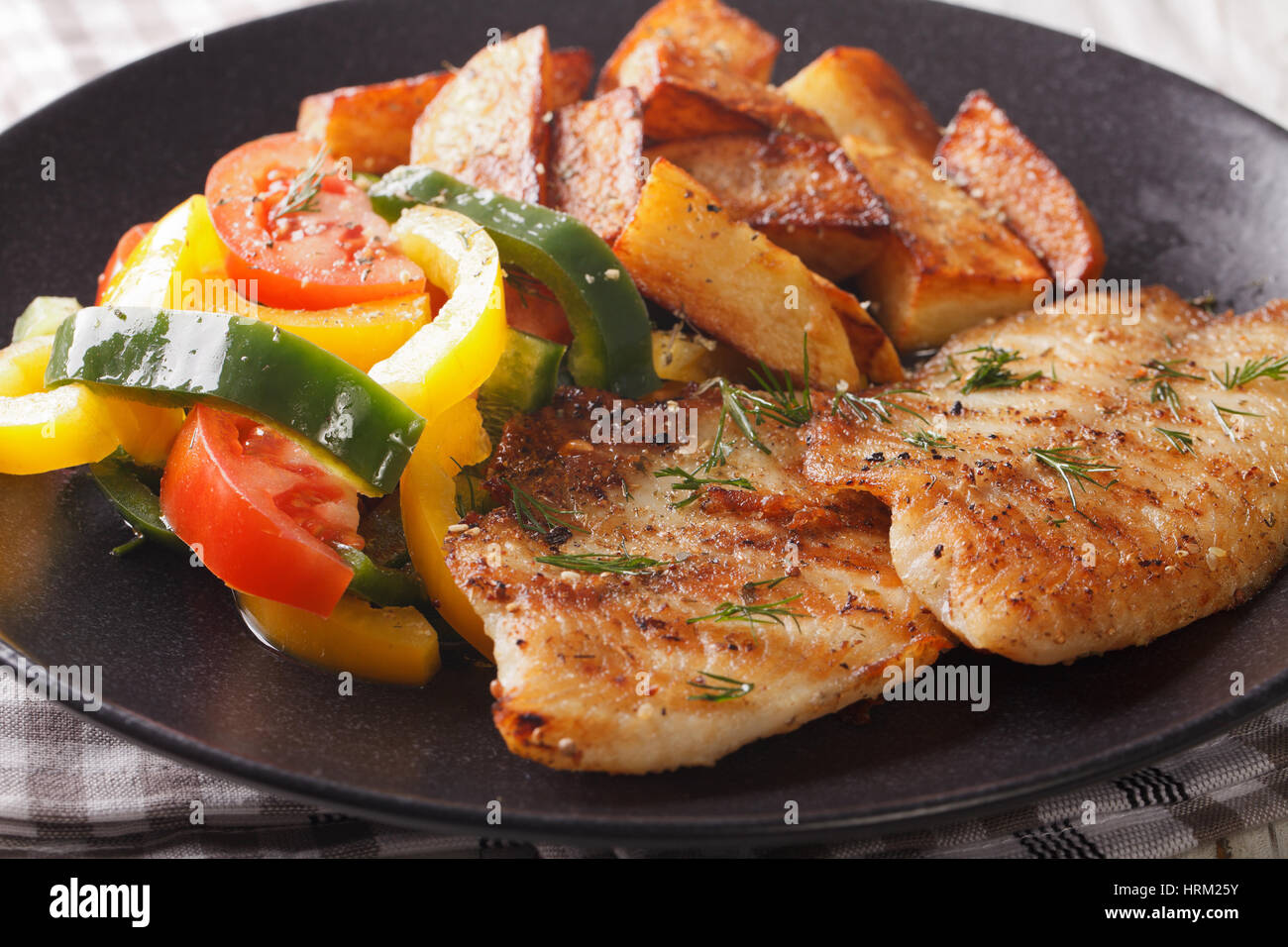 Grilled Tilapia fillet and potato wedges, fresh salad on a plate close ...