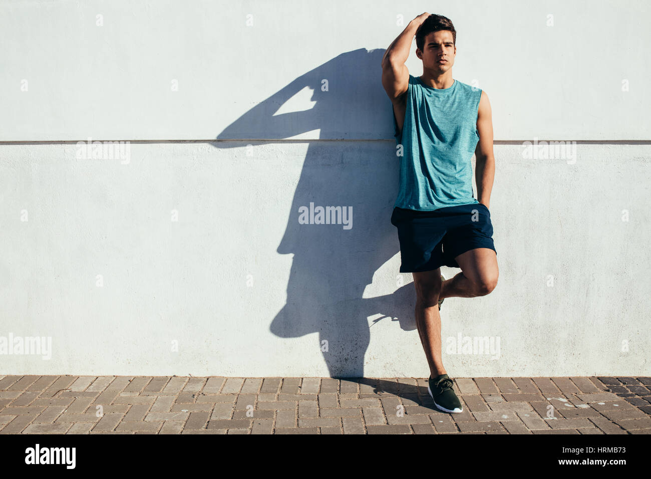 Full length shot of fit young man standing against a wall outdoors ...