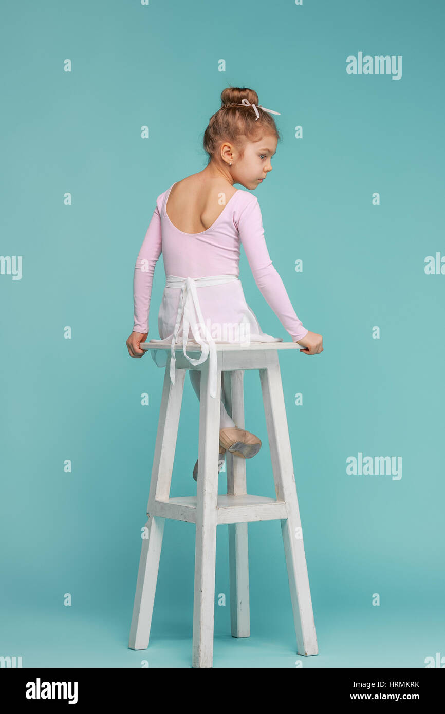 The back view of little girl as balerina dancer sitting on white wooden ...