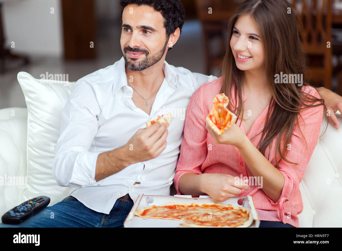 Happy couple watching tv while eating pizza Stock Photo - Alamy