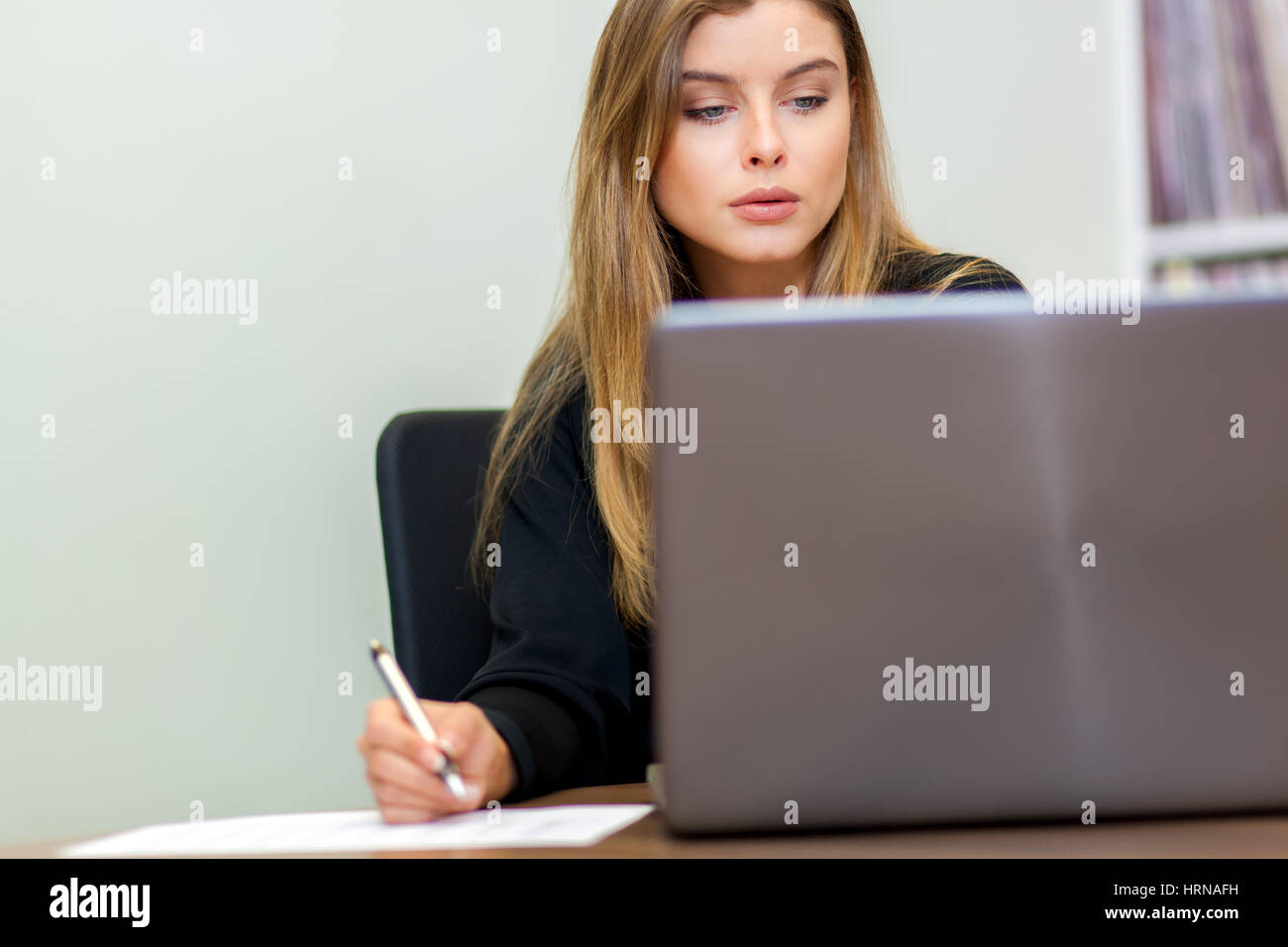 Woman using a laptop computer and writing in her office Stock Photo - Alamy