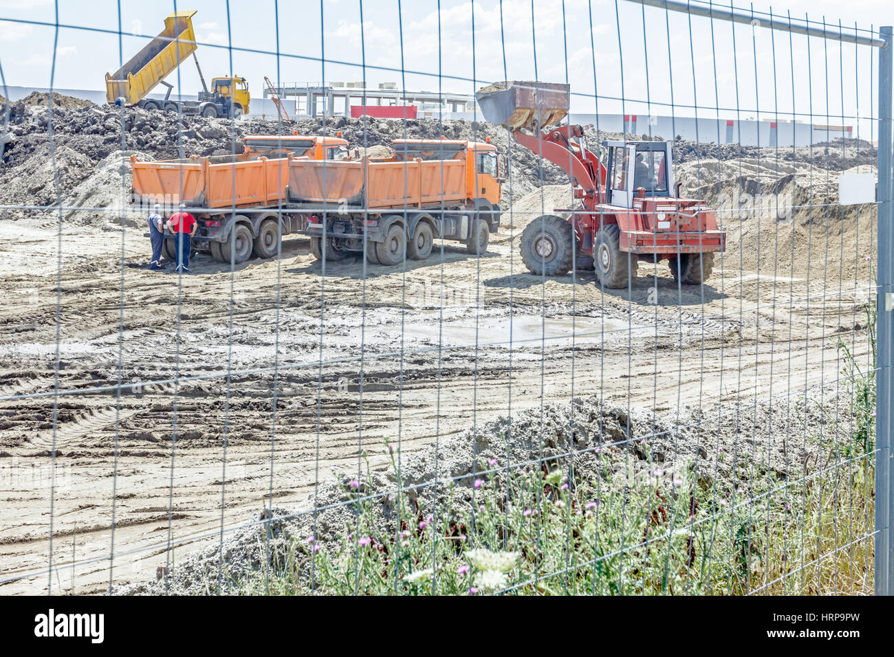 View through a fence wire on big loader until is filling a dump truck ...
