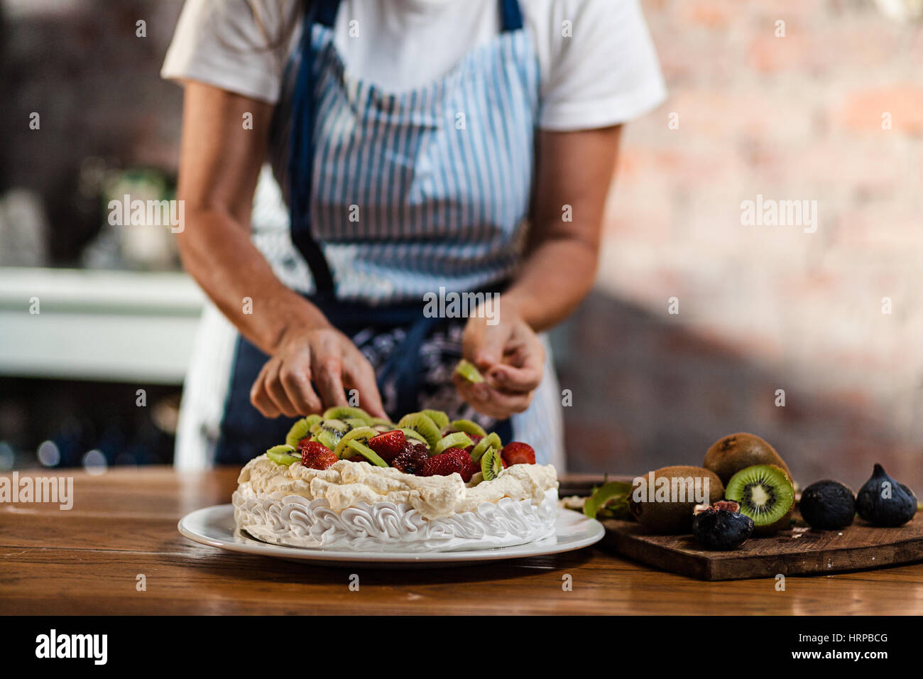 Woman in a cottage-style kitchen sifting icing sugar over a pavlova ...