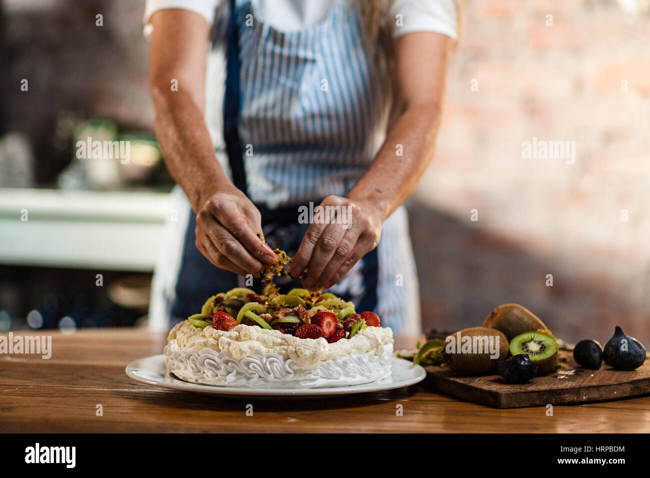 Woman in a cottage-style kitchen sifting icing sugar over a pavlova ...