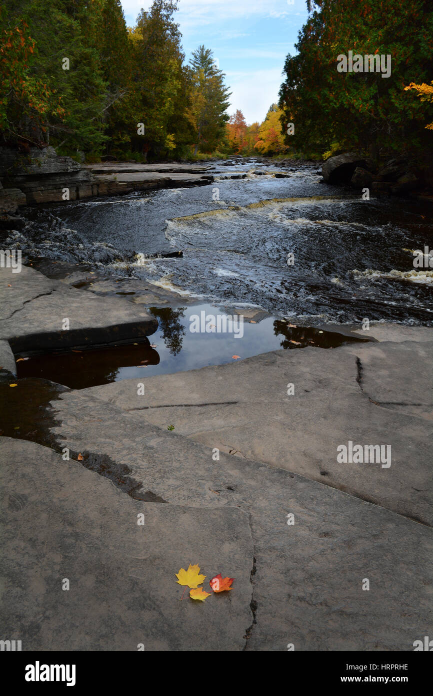 Looking down a river in autumn with flat rocks and three colorful ...