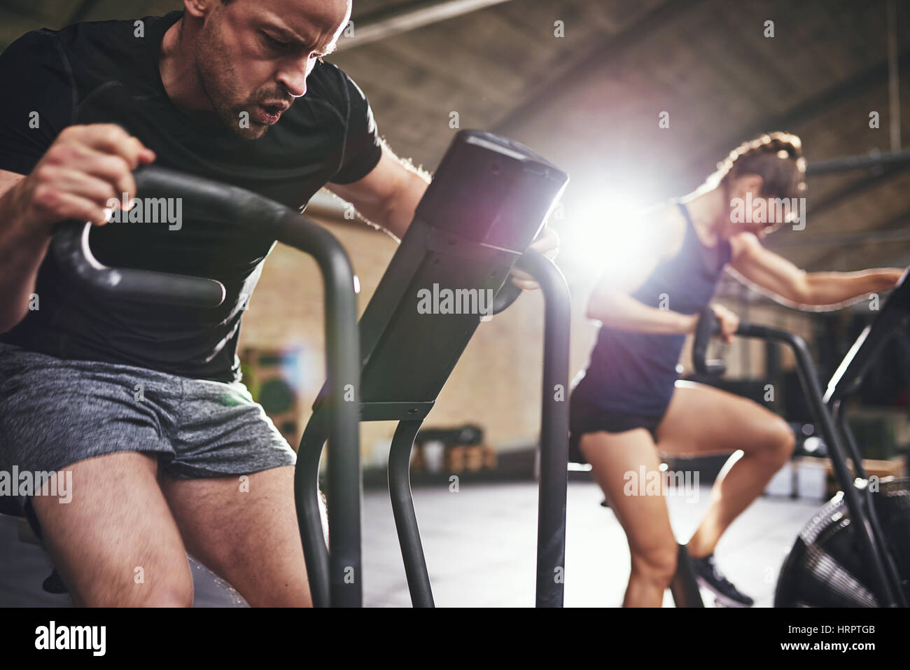 Young man and woman grimacing and riding cycling machines in hard ...