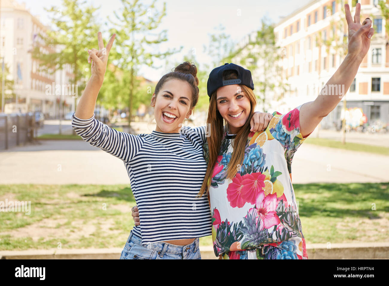 Two happy young female students making v-signs as they stand arm in arm ...