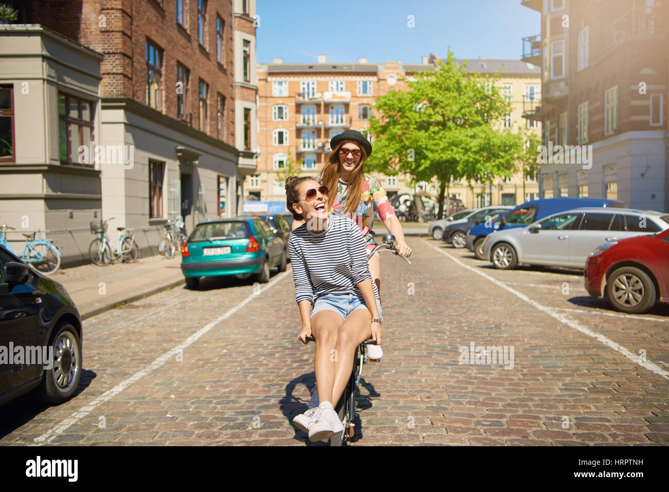 Teenage female in black hat riding on bike with friend outside going in ...