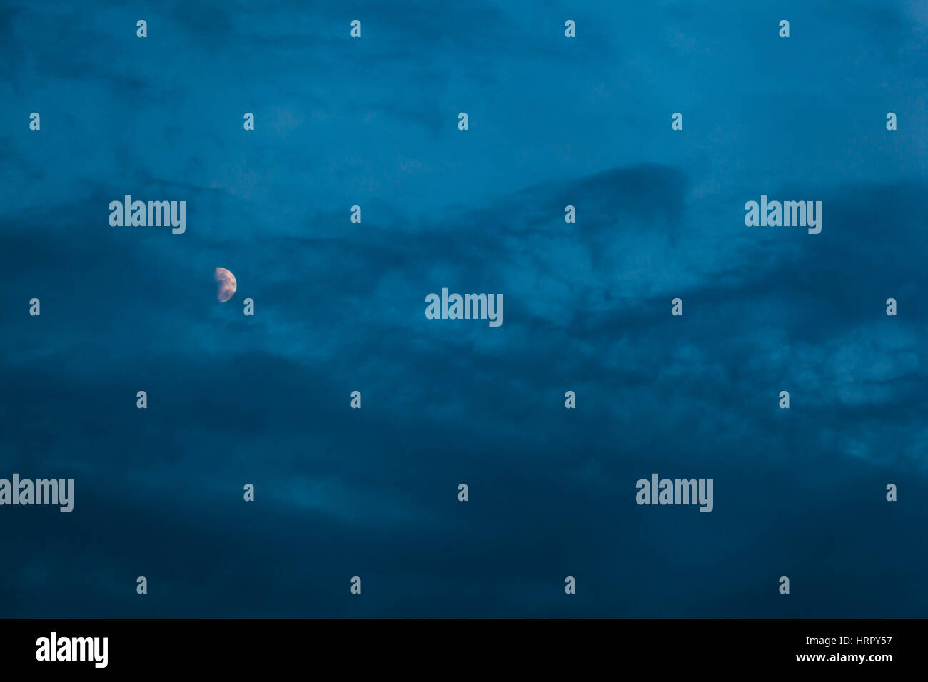 Half moon under the clouds in the evening Stock Photo - Alamy