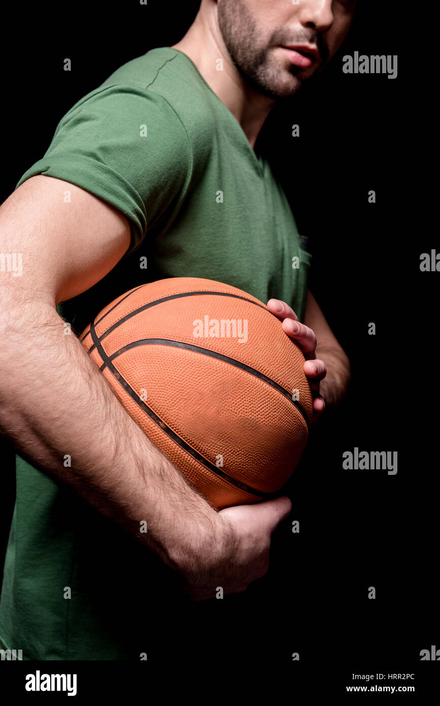 partial side view of man holding basketball ball in hands on black ...