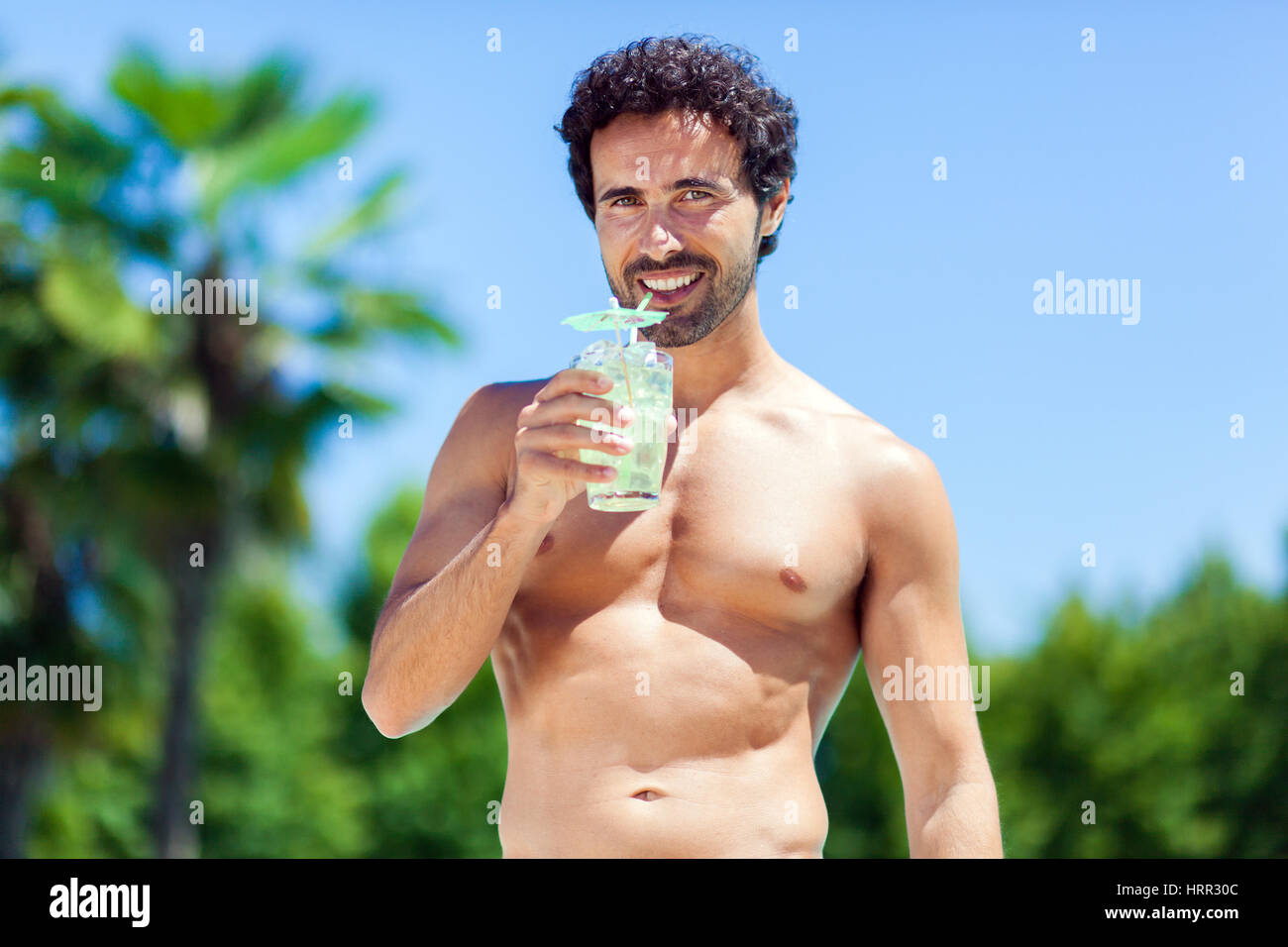 Handsome young man drinking a cocktail while relaxing in a swimming ...