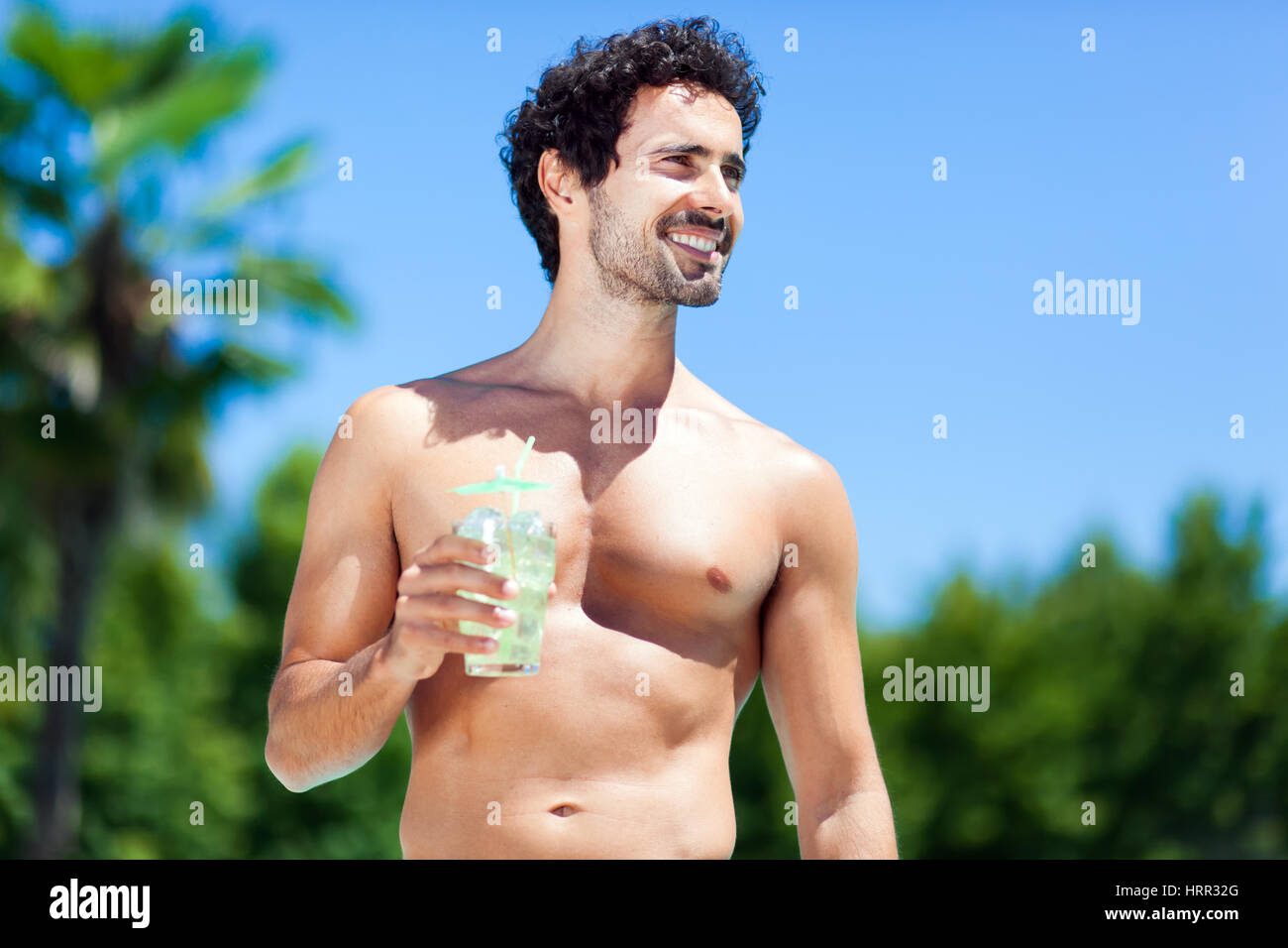 Handsome young man drinking a cocktail while relaxing in a swimming ...