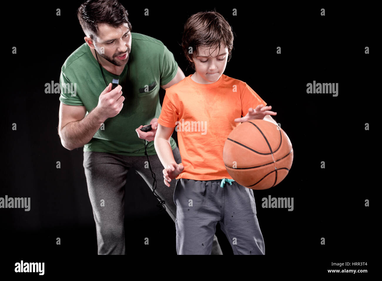 man controlling time while concentrated boy training with basketball ...