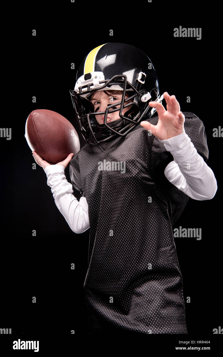 Angry little boy in uniform playing american football on black Stock ...