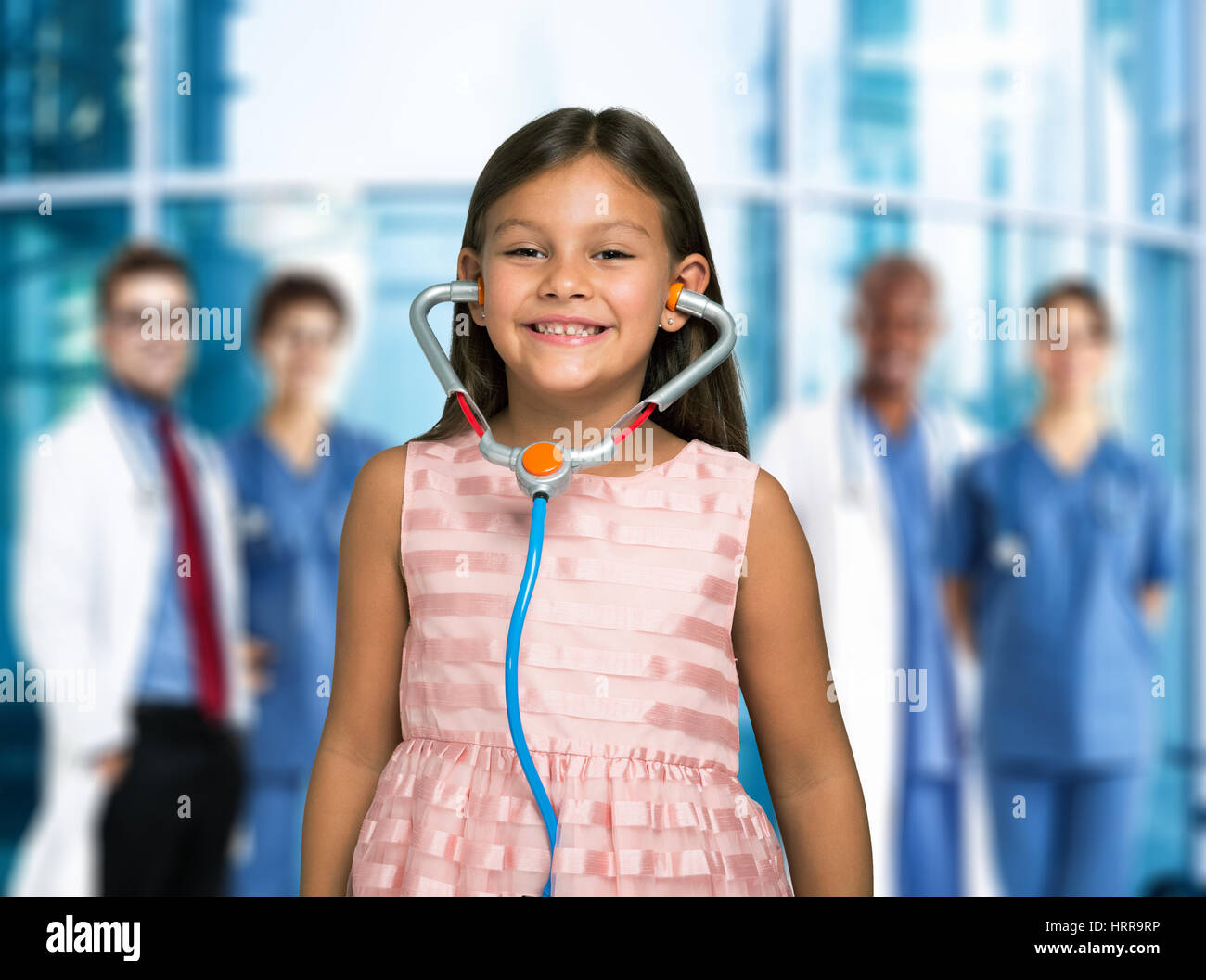 Smiling child using a toy stethoscope in front of a group of doctors ...
