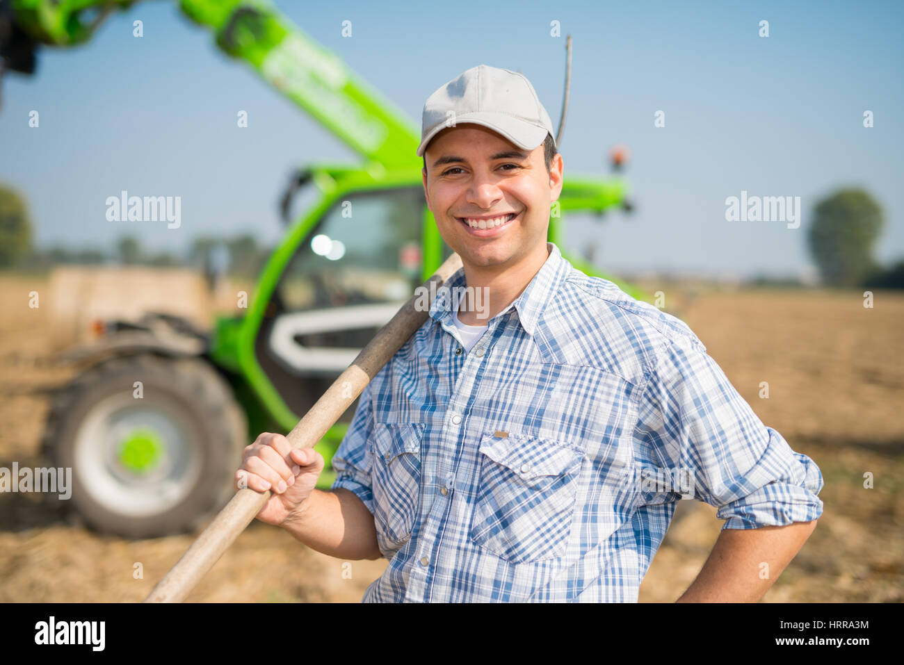 Portrait of a smiling farmer holding a pitchfork while working in his ...