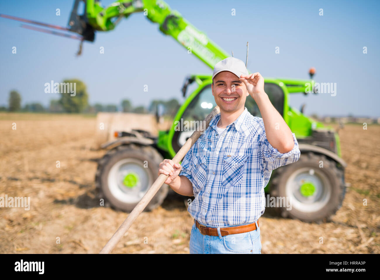 Portrait of a smiling farmer holding a pitchfork while working in his ...