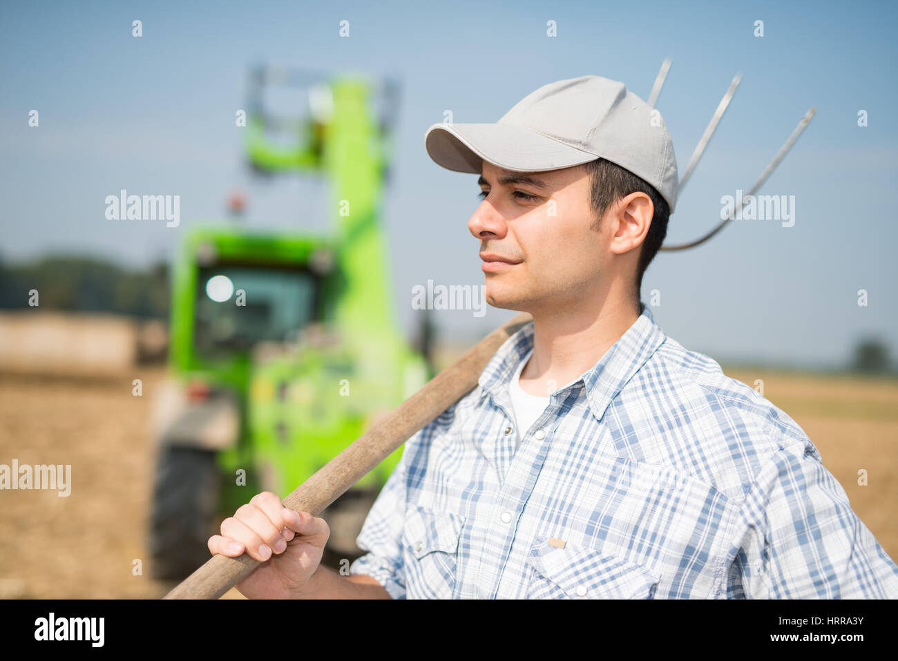 Portrait of a smiling farmer holding a pitchfork while working in his ...