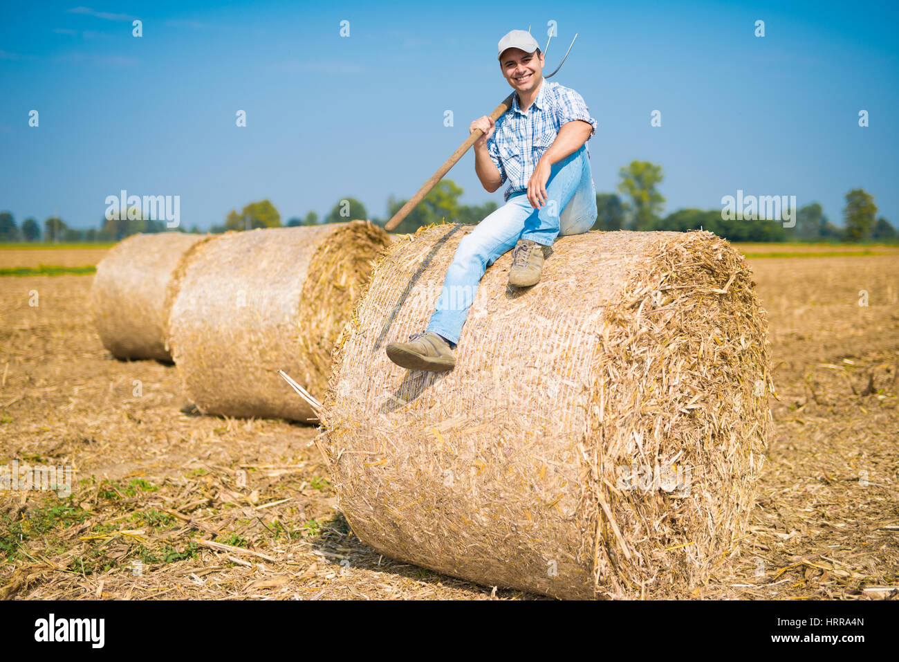 Portrait of a smiling farmer sitting on an hay bale in his field Stock ...