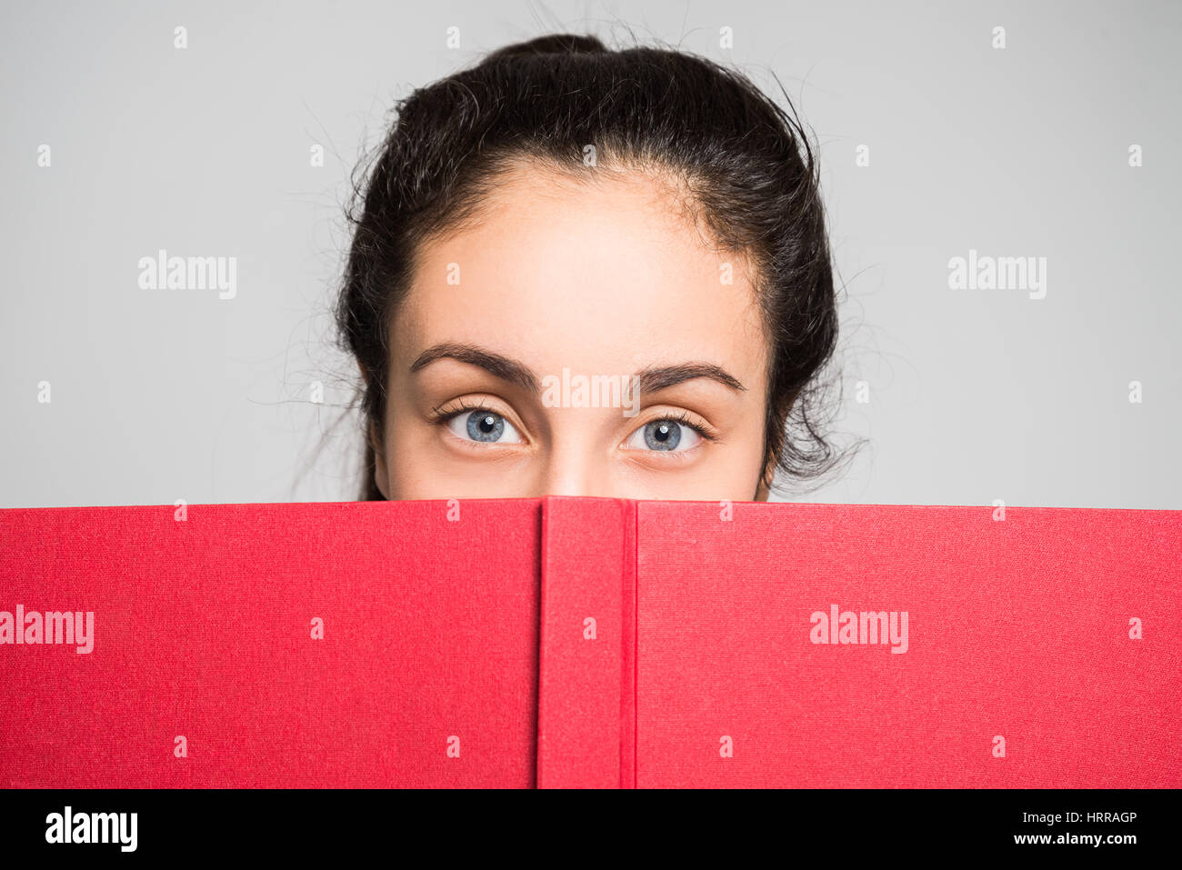 Teen looking from behind a book Stock Photo - Alamy
