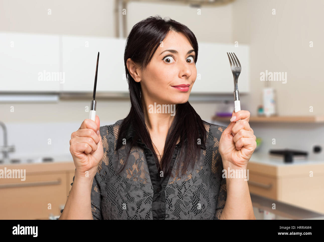 Hungry woman holding fork and knife in her kitchen Stock Photo - Alamy