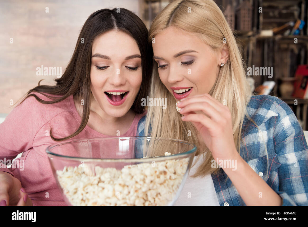 Excited attractive young women eating popcorn from glass bowl Stock ...