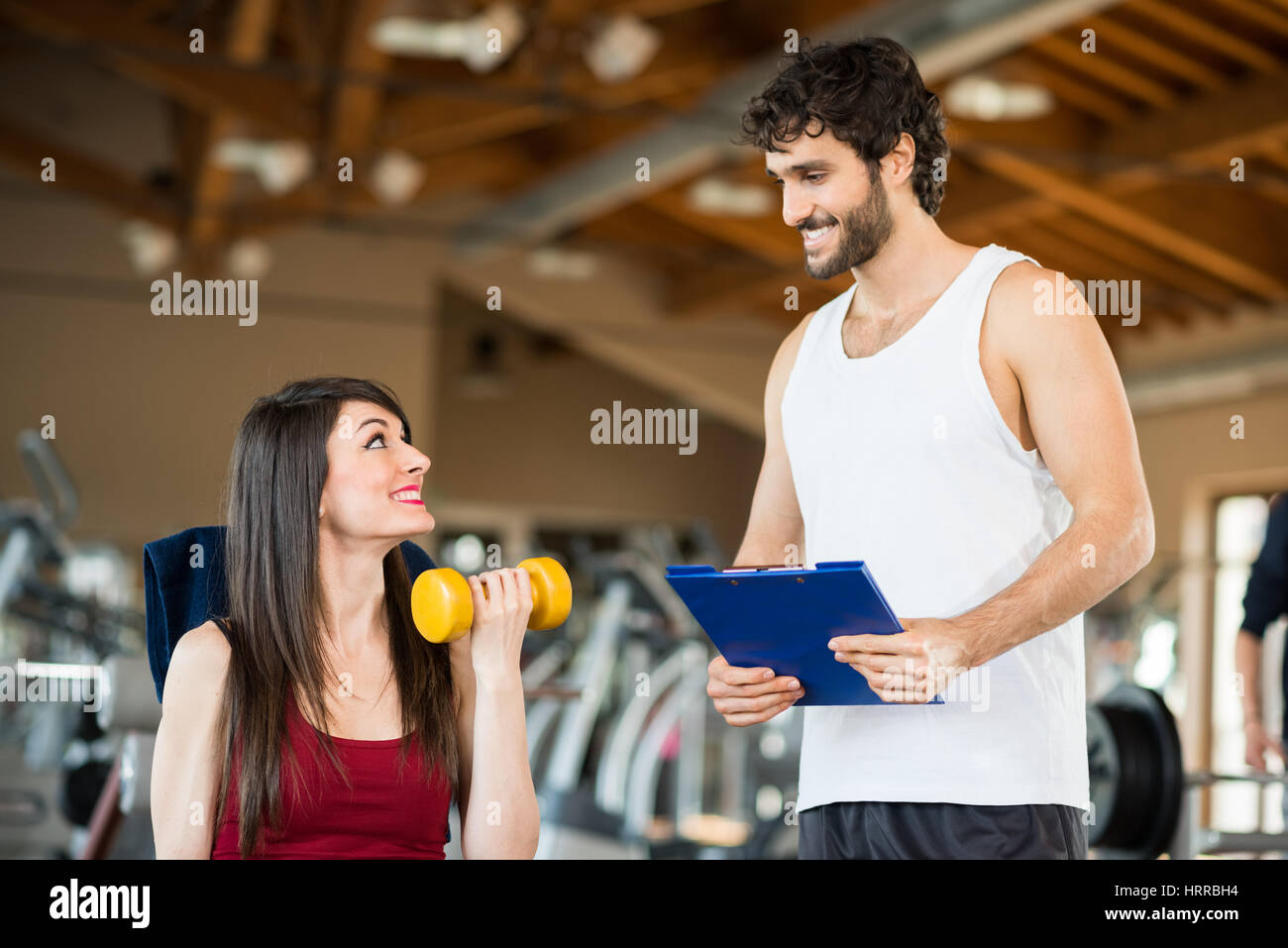 Woman working out in a gym while her personal trainer looks at the ...
