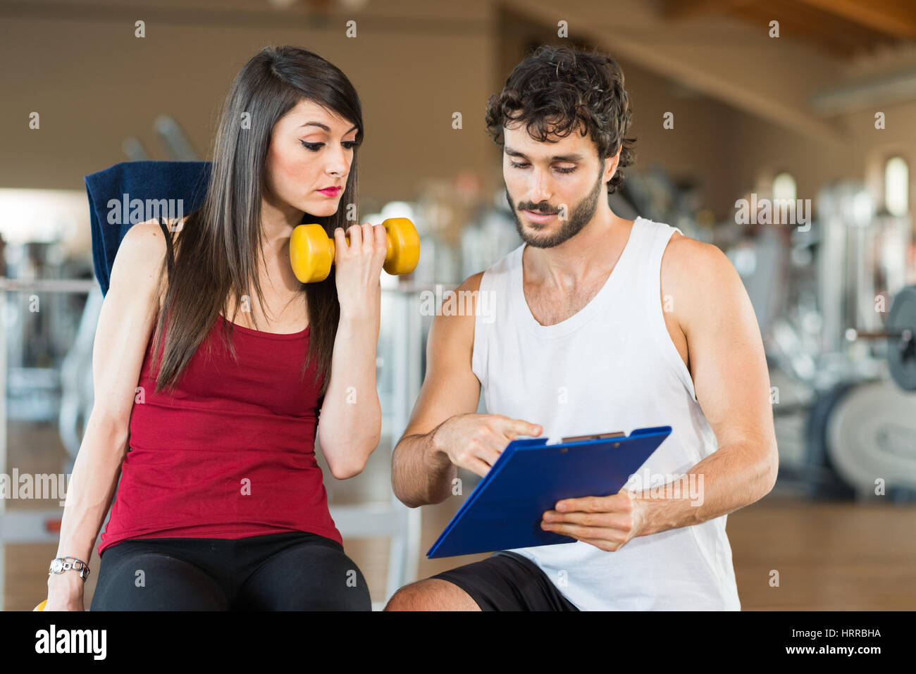 Woman working out in a gym while her personal trainer looks at the ...