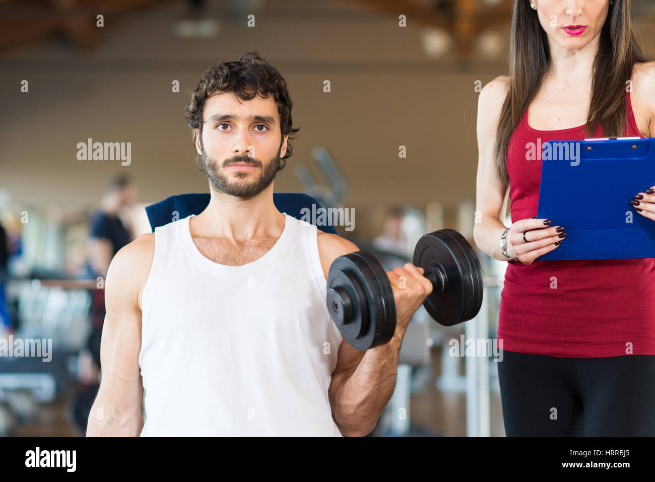 Man working out in a gym while his personal trainer looks at the ...