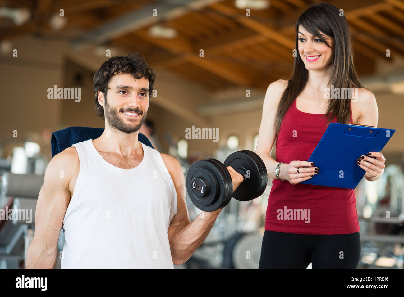 Man working out in a gym while his personal trainer looks at the ...