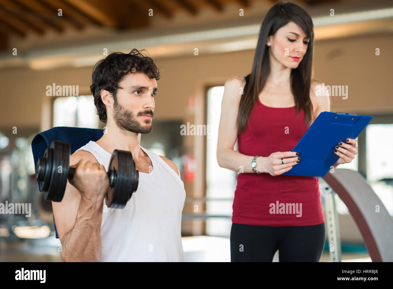 Man working out in a gym while his personal trainer looks at the ...