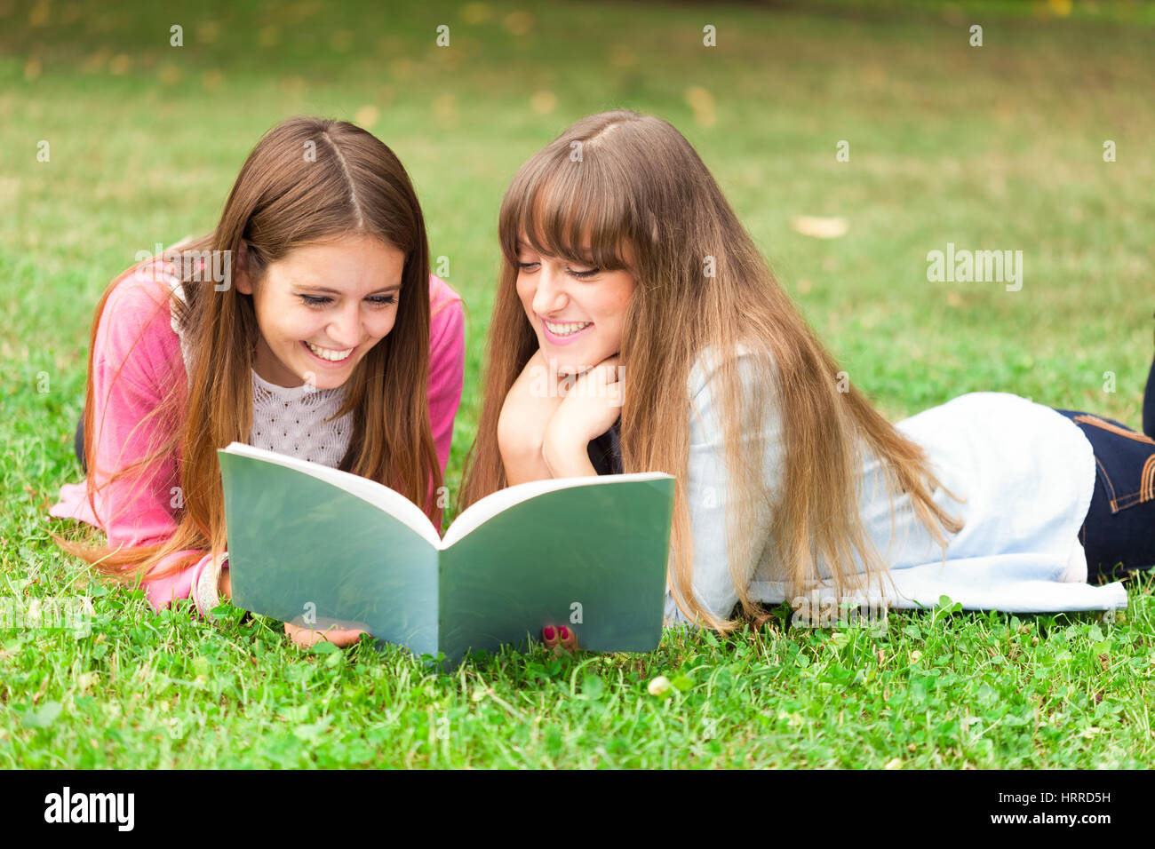 Girls reading a notebook together while lying down on the grass Stock ...