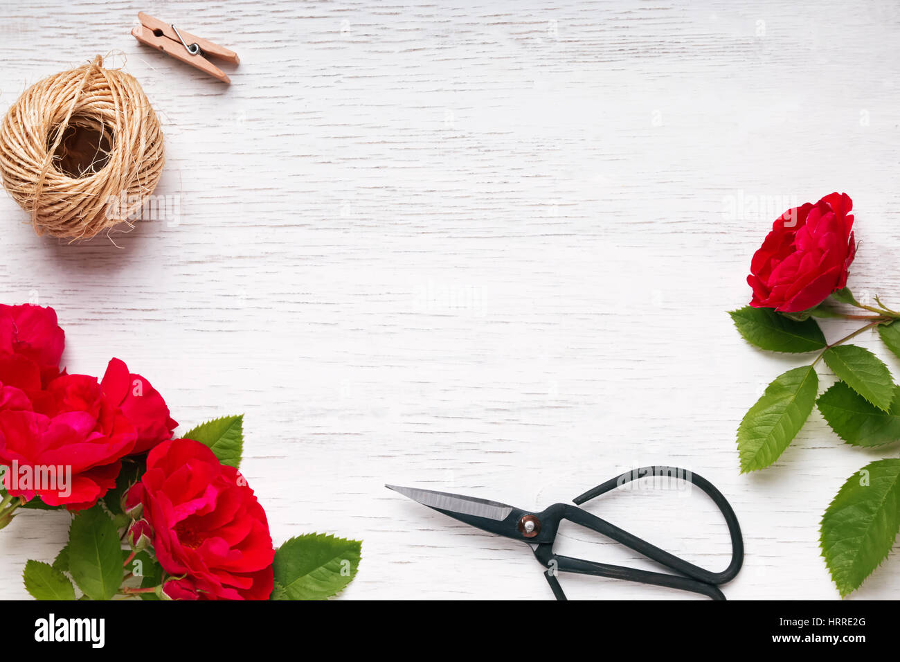Red roses, jute rope and scissors on the white wooden table, top view ...