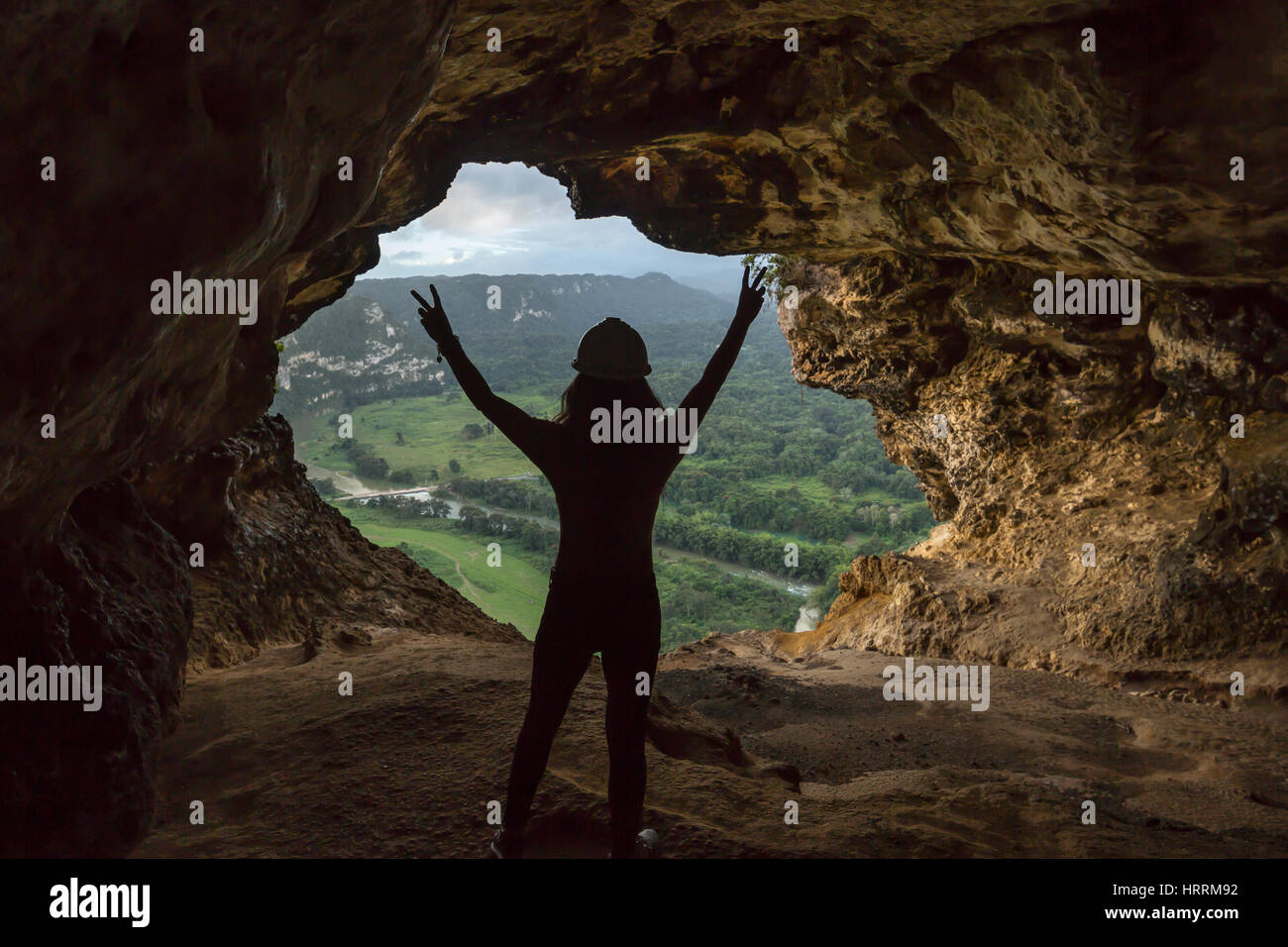 YOUNG WOMAN STANDS RAISING ARMS IN VICTORY CAVE WINDOW OVERLOOKING RIO ...