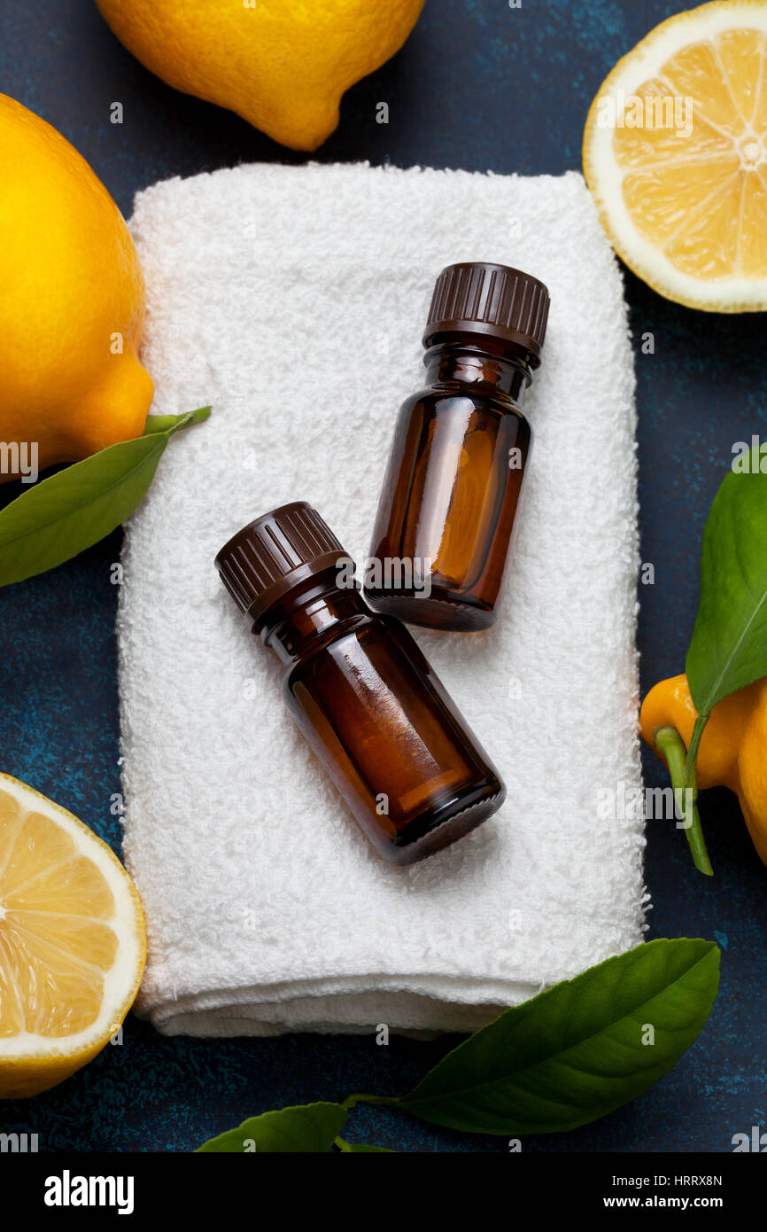 two bottles of lemon essential oil on a white towel, and fresh lemons ...