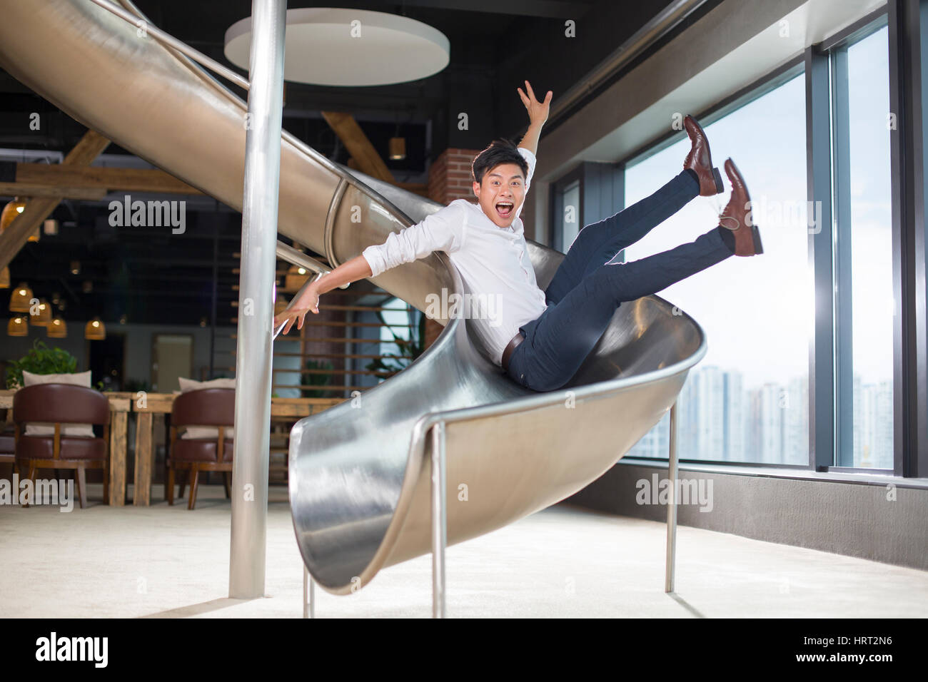 Young businessman playing on slide Stock Photo - Alamy