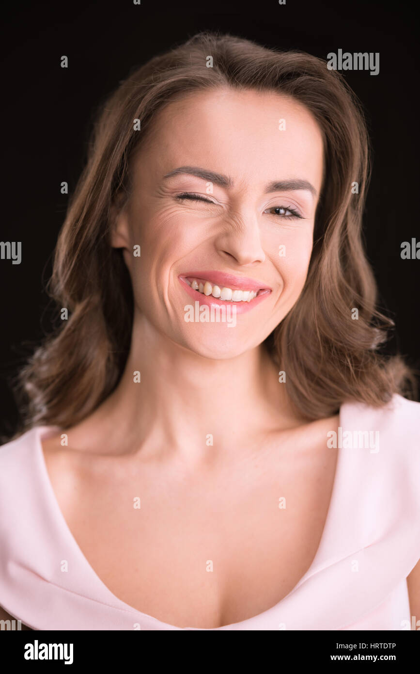 Portrait of beautiful young brunette woman winking on black Stock Photo ...