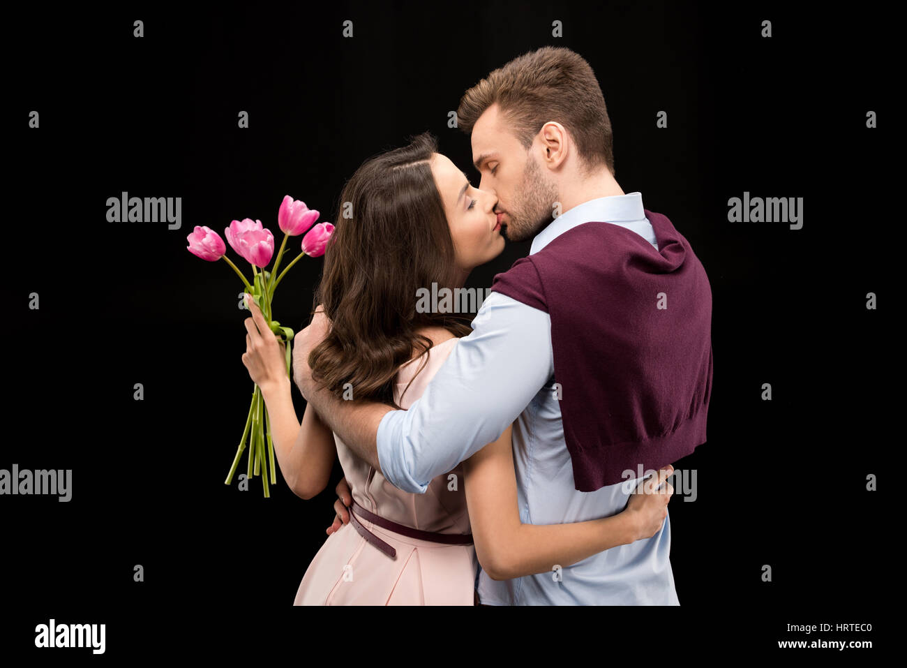 back view of man kissing woman with tulips bouquet on black ...