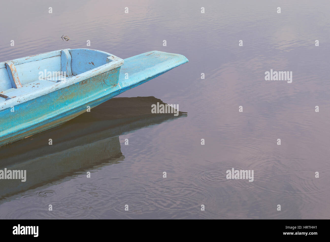 One old blue wooden boat, with its reflection on the calm water, lonely ...