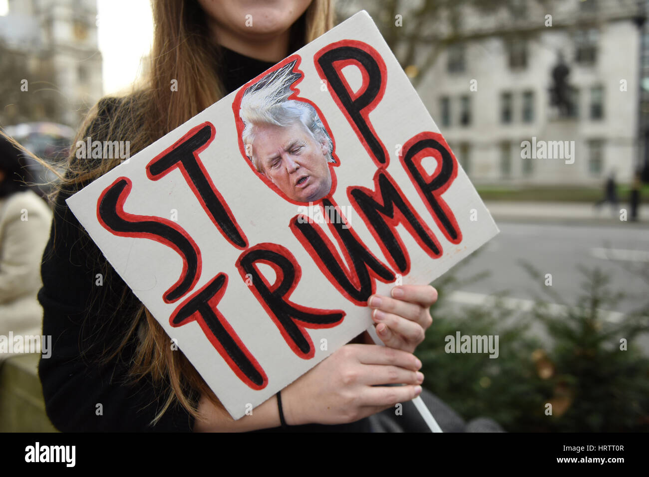 A young woman is holding a handmade placard reading: "Stop Trump ...