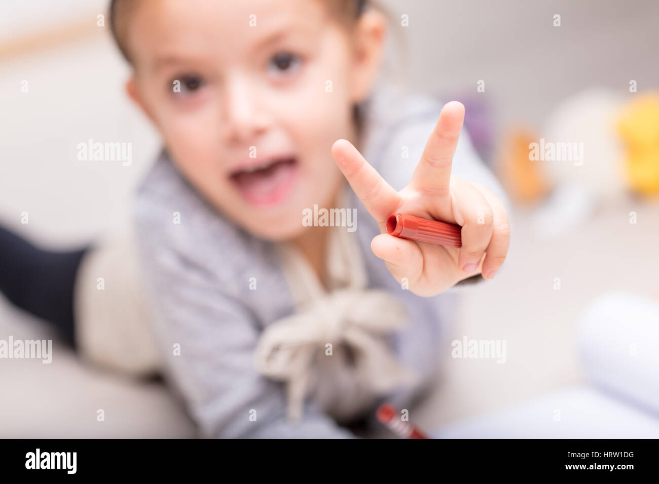 Fun little girl making a V-sign gesture with her fingers while holding ...