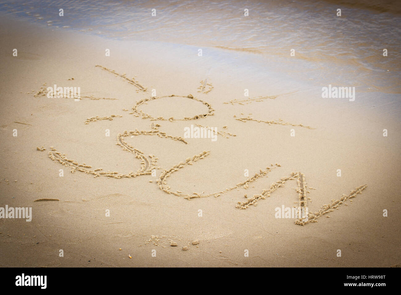 Word sun and shape of sun written on sand at the beach by the sea ...
