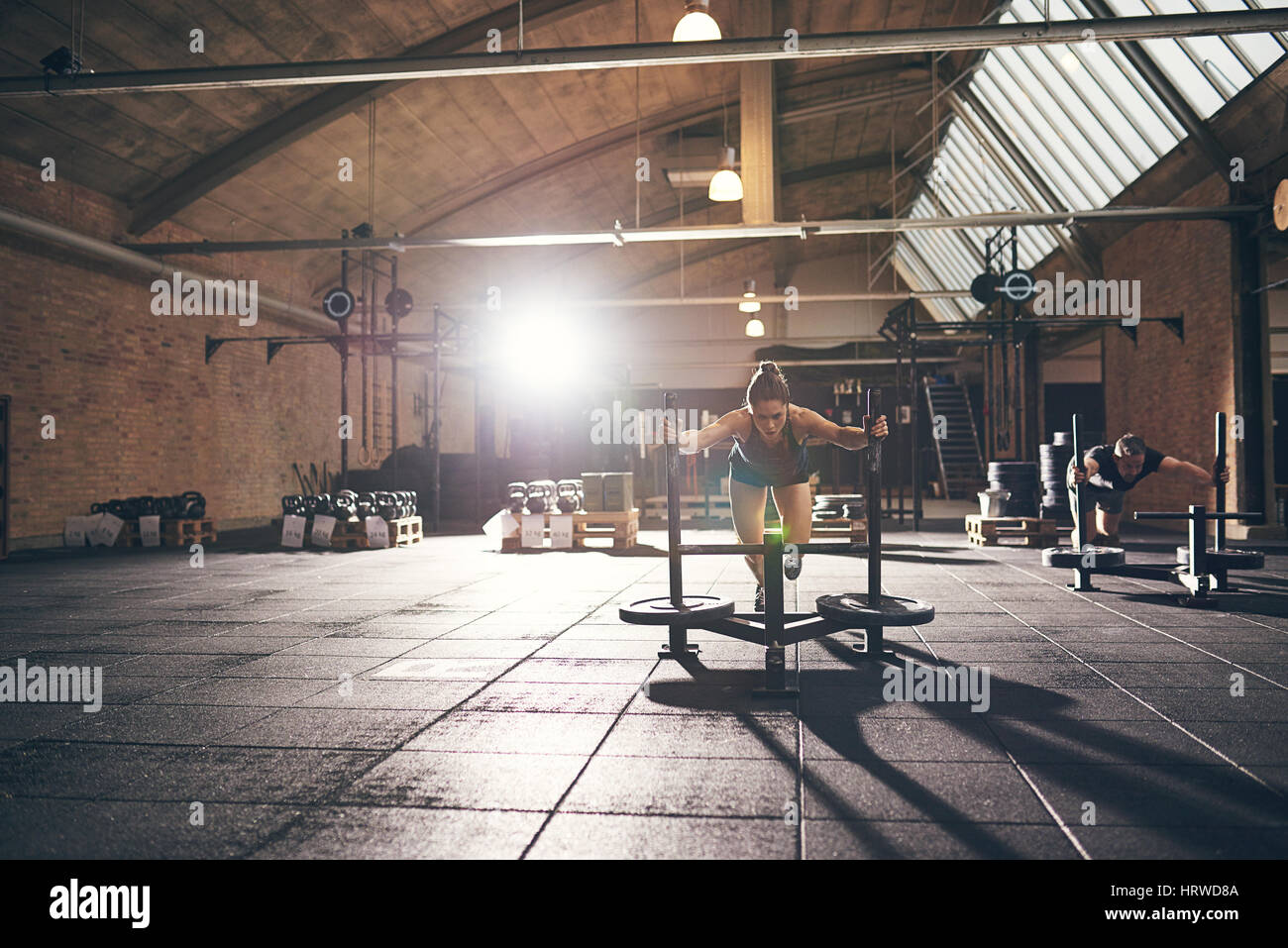 Strong woman pushing metal bogie with weight disks in gym. Horizontal ...